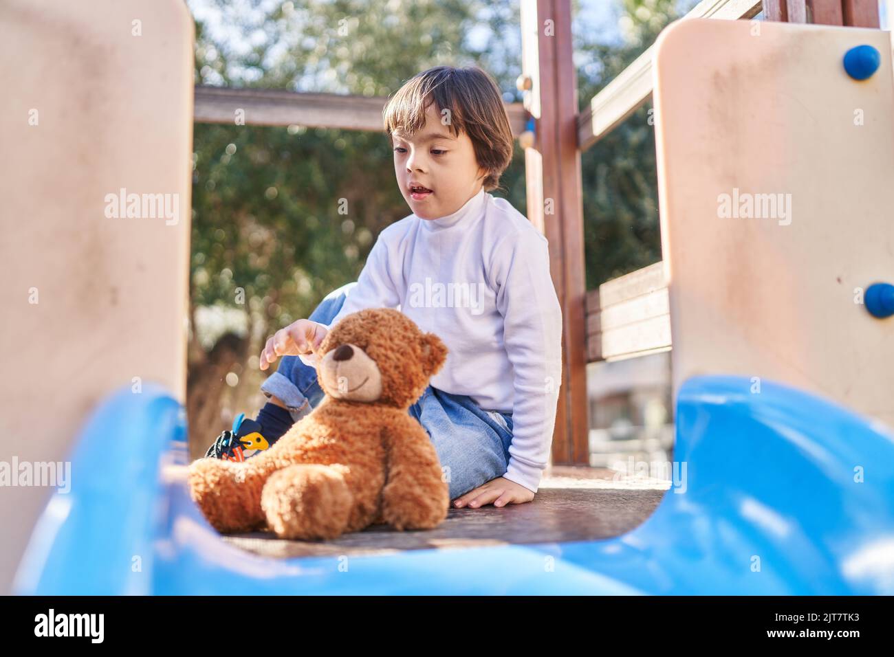 Down syndrome kid playing with teddy bear on slide at park Stock Photo ...