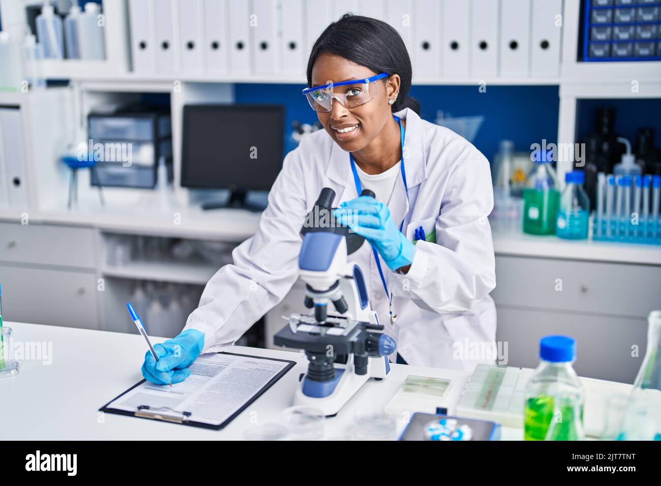 Young african american woman scientist using microscope write on document at laboratory Stock ...