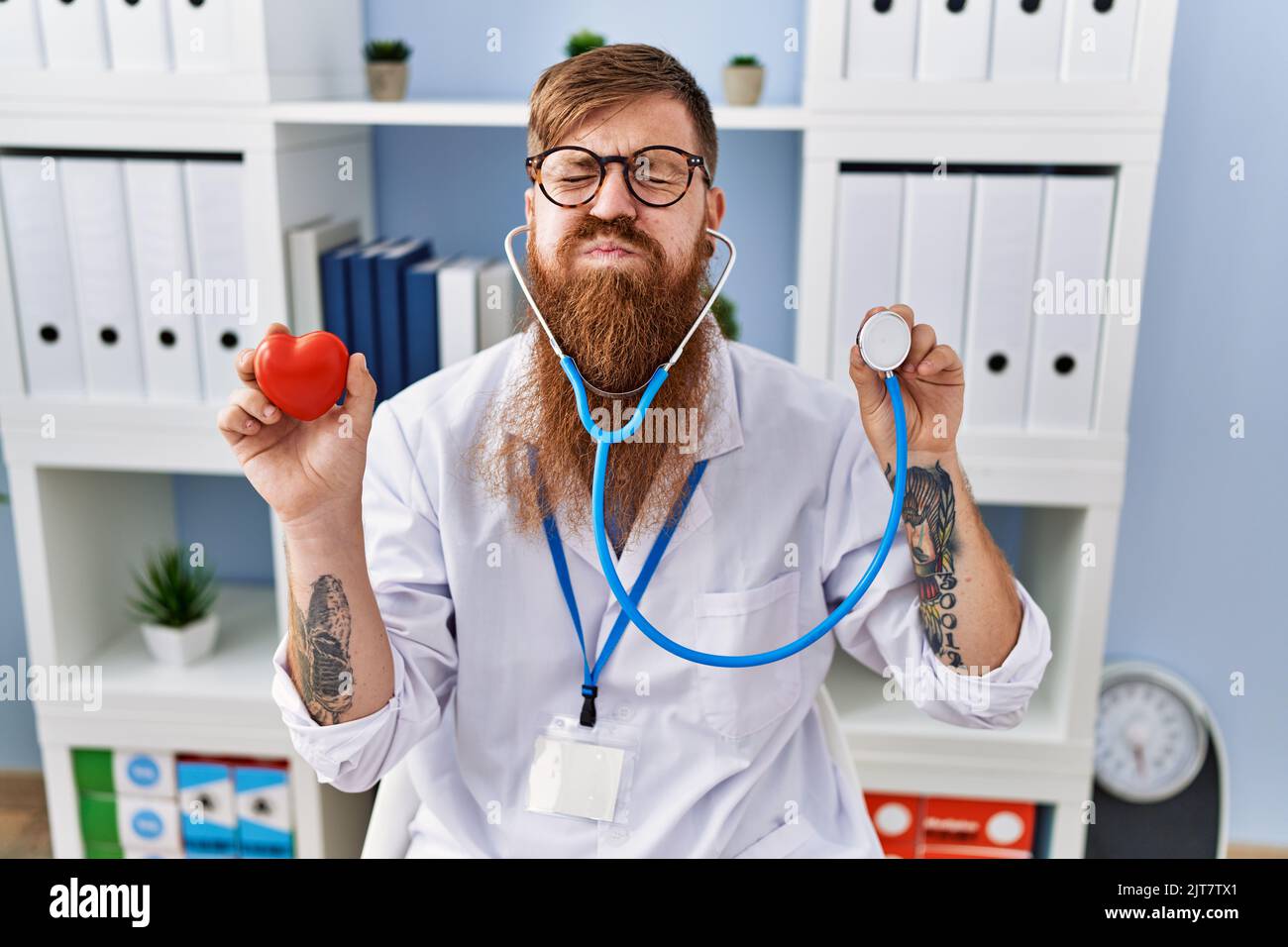 Redhead Man With Long Beard Wearing Doctor Uniform Holding Heart And