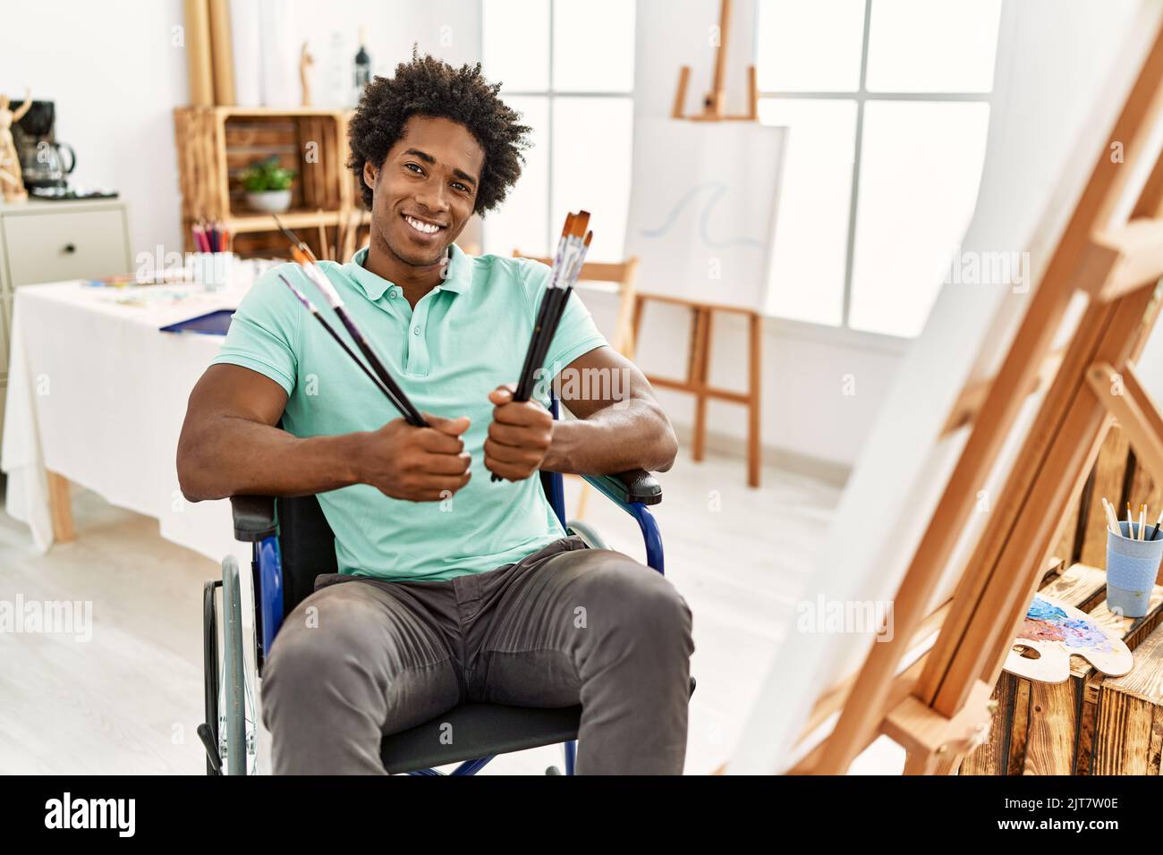 Young african american disabled artist man holding paintbrushes sitting ...