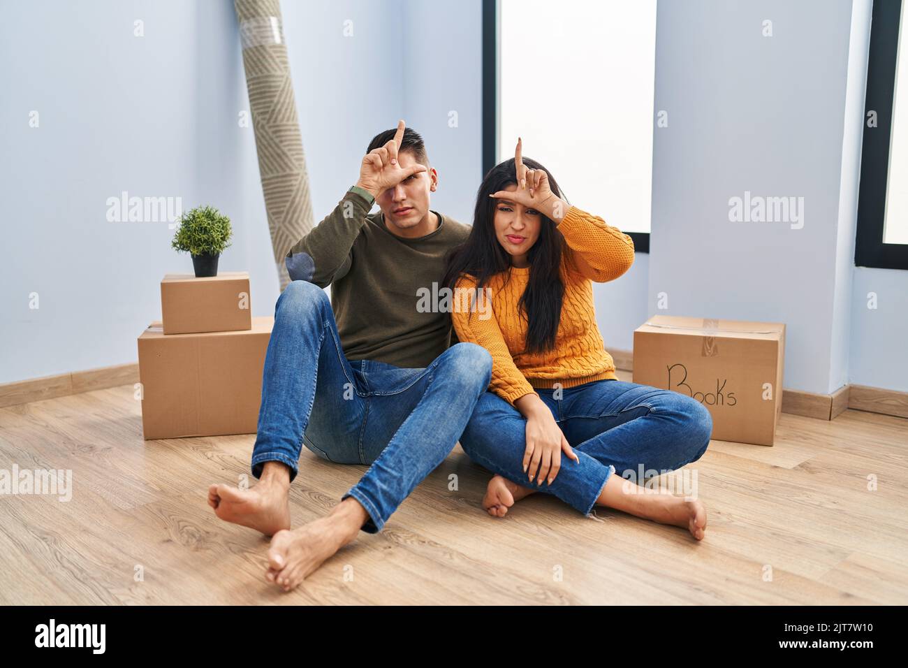 Young couple sitting on the floor at new home making fun of people with ...