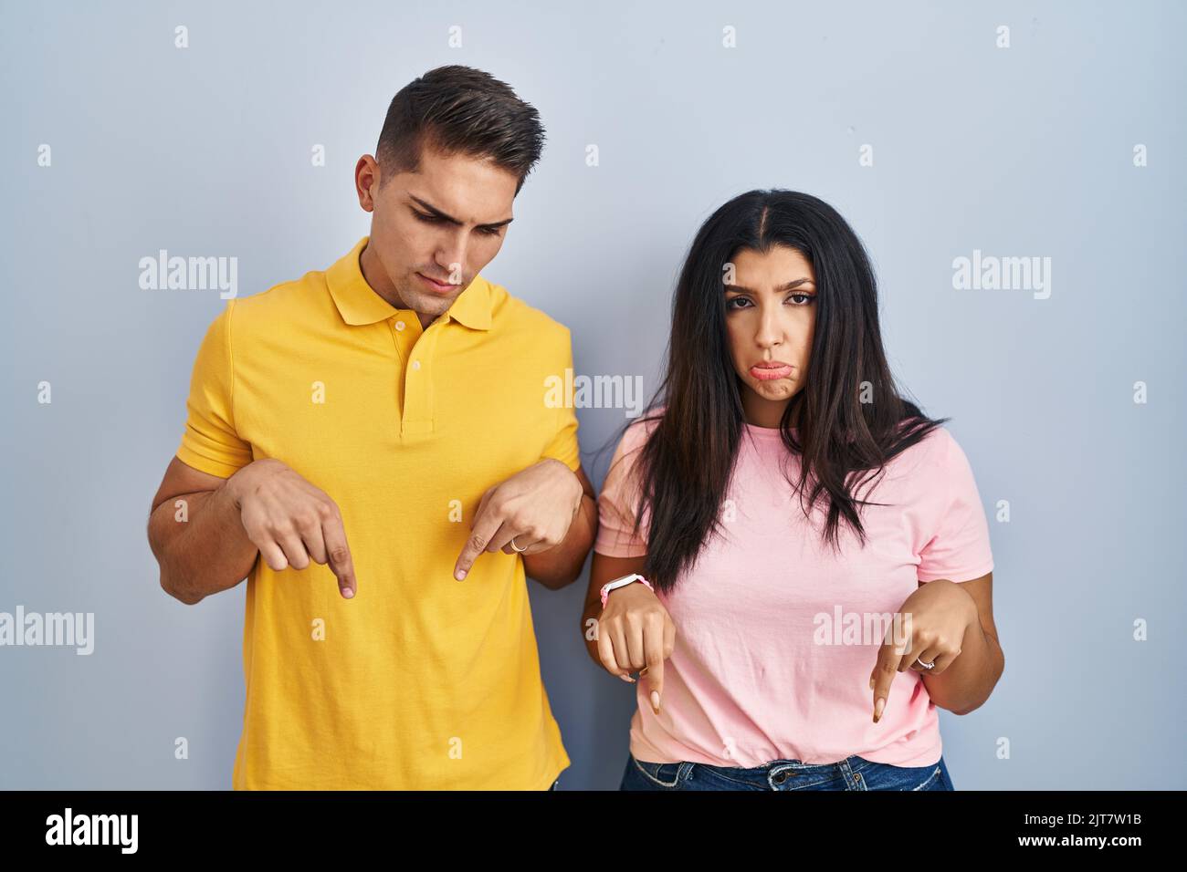 Young couple standing over isolated background pointing down looking ...