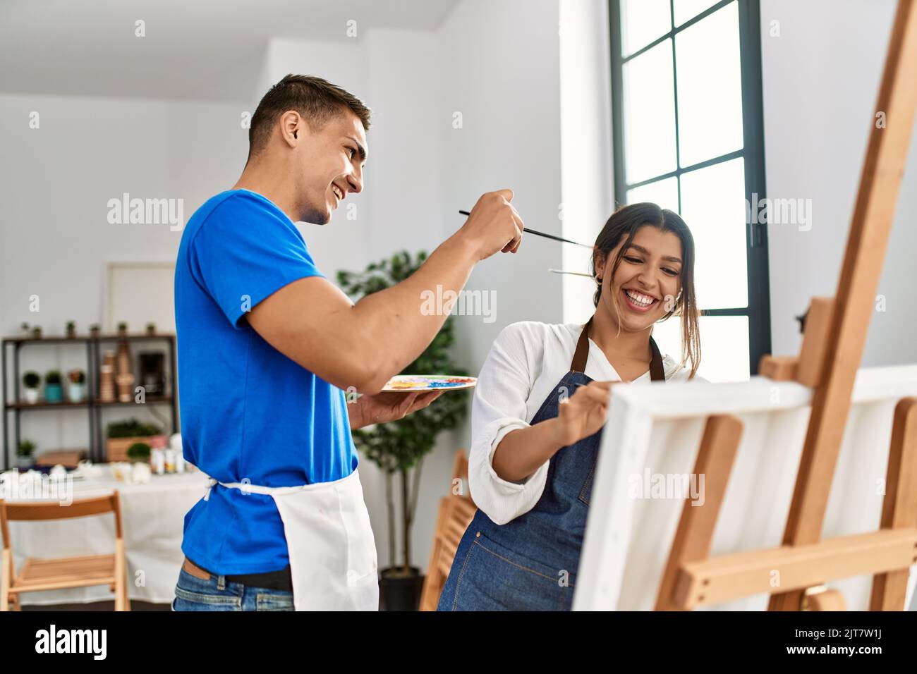 Two students smiling happy playing with paintbrush painting to each ...