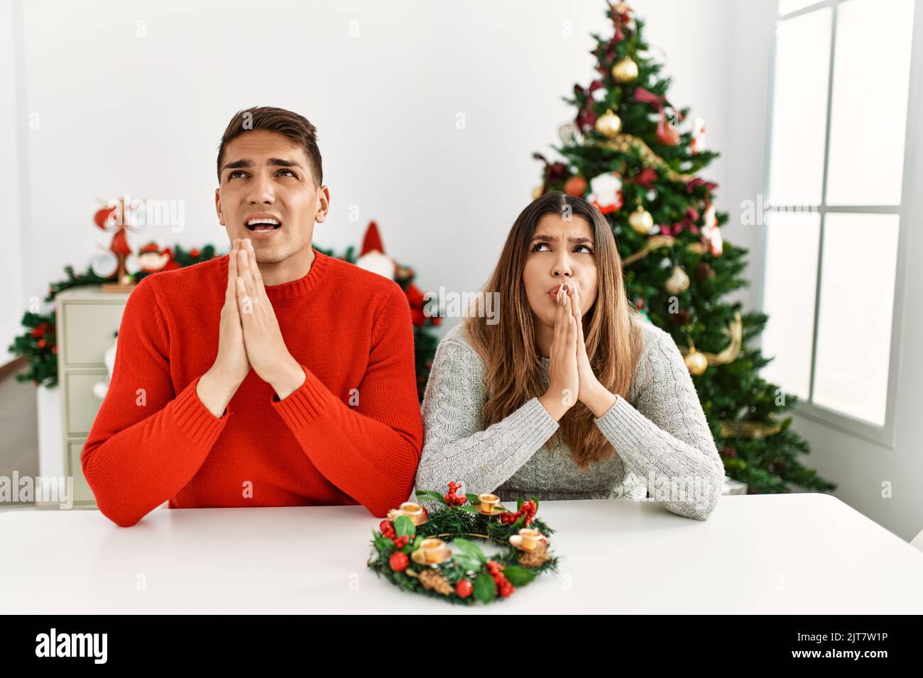 Young hispanic couple sitting at the table on christmas begging and ...