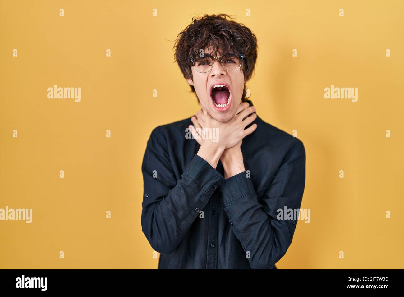 Young man wearing glasses over yellow background shouting and suffocate ...