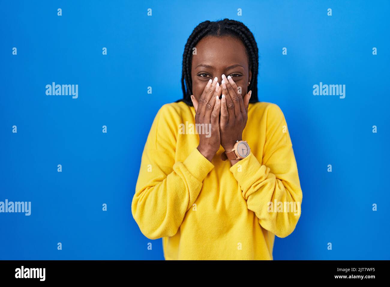 Beautiful black woman standing over blue background laughing and ...