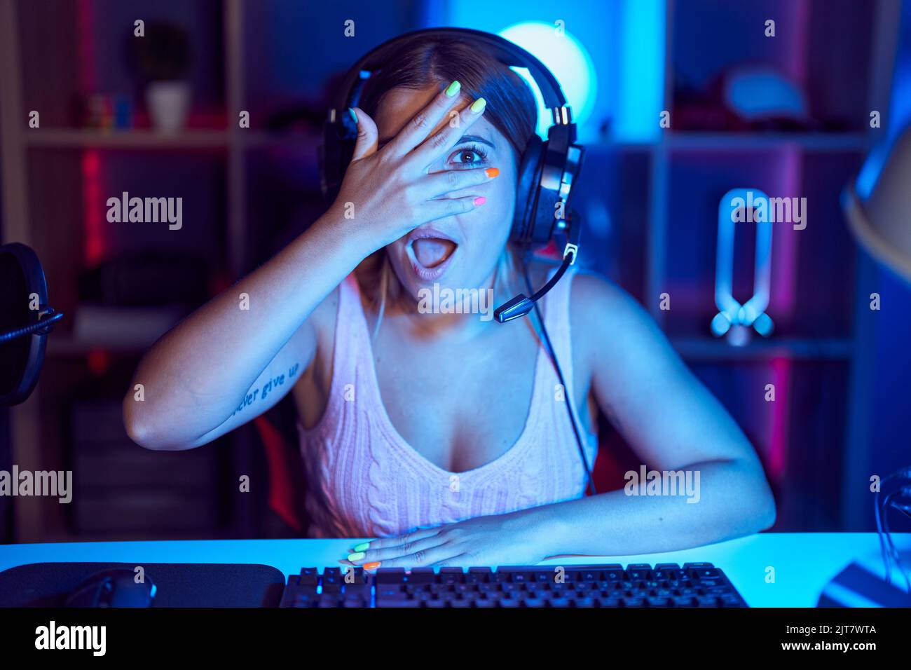 Young blonde woman playing video games wearing headphones peeking in ...