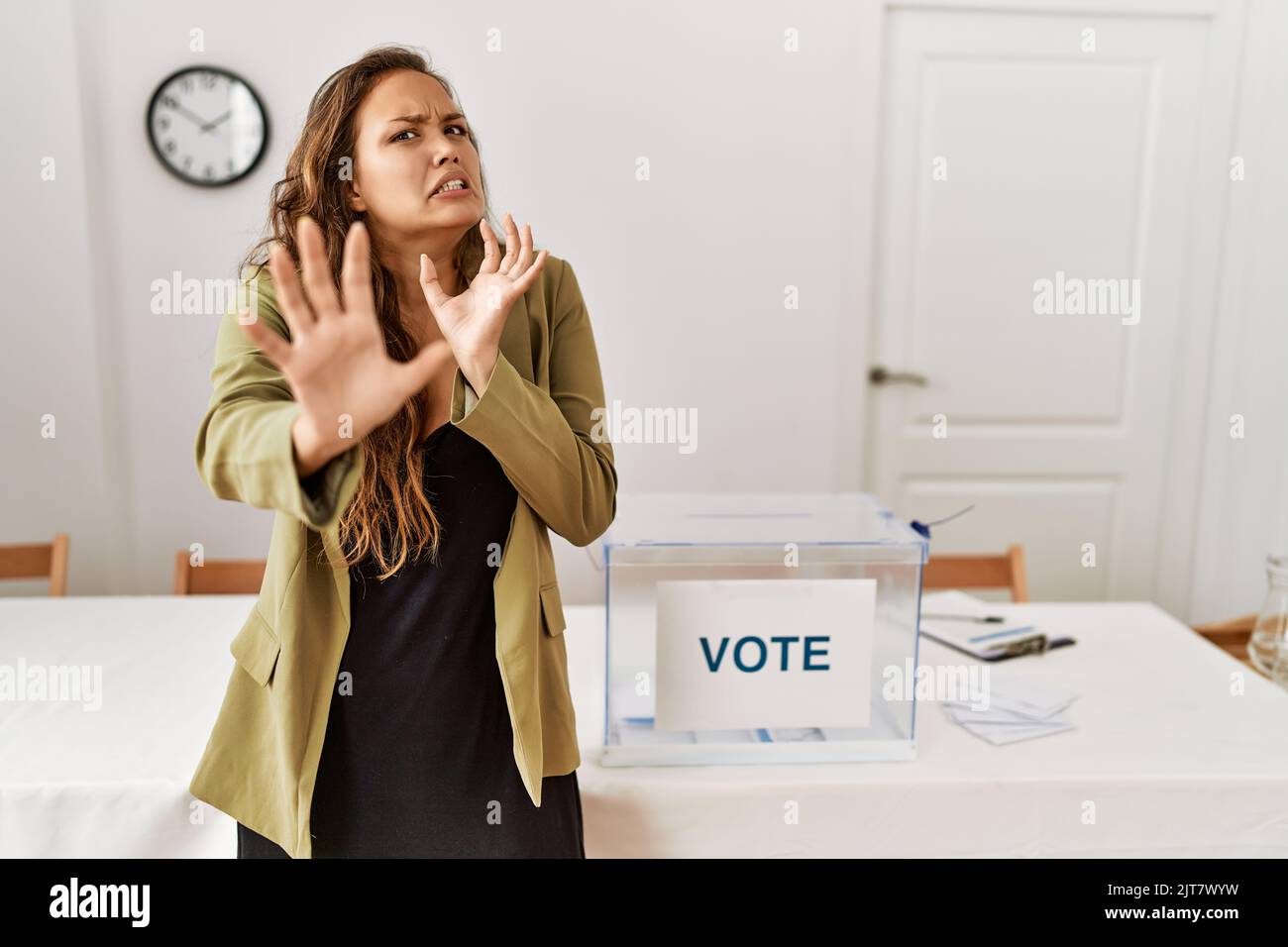 Beautiful hispanic woman standing at political campaign room afraid and ...