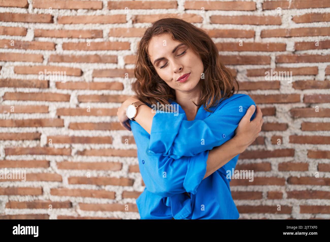 Beautiful brunette woman standing over bricks wall hugging oneself ...