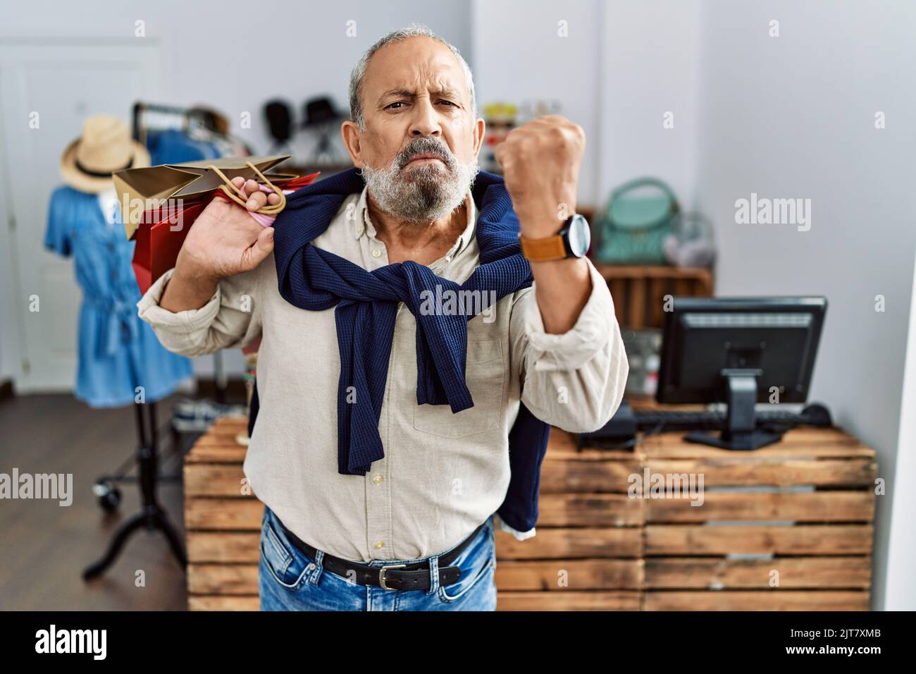 Handsome senior man holding shopping bags at boutique shop angry and ...