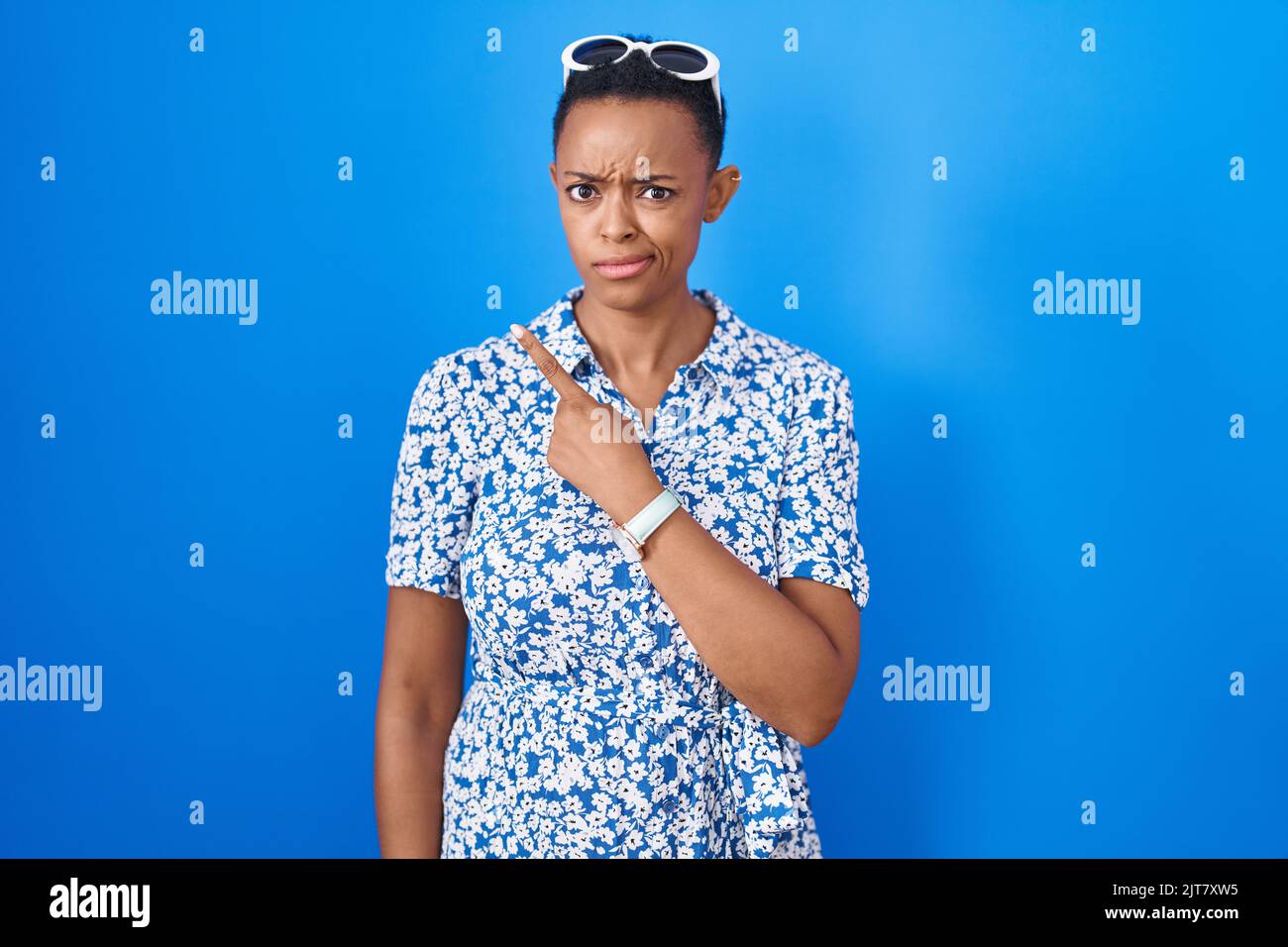 African american woman standing over blue background pointing aside ...