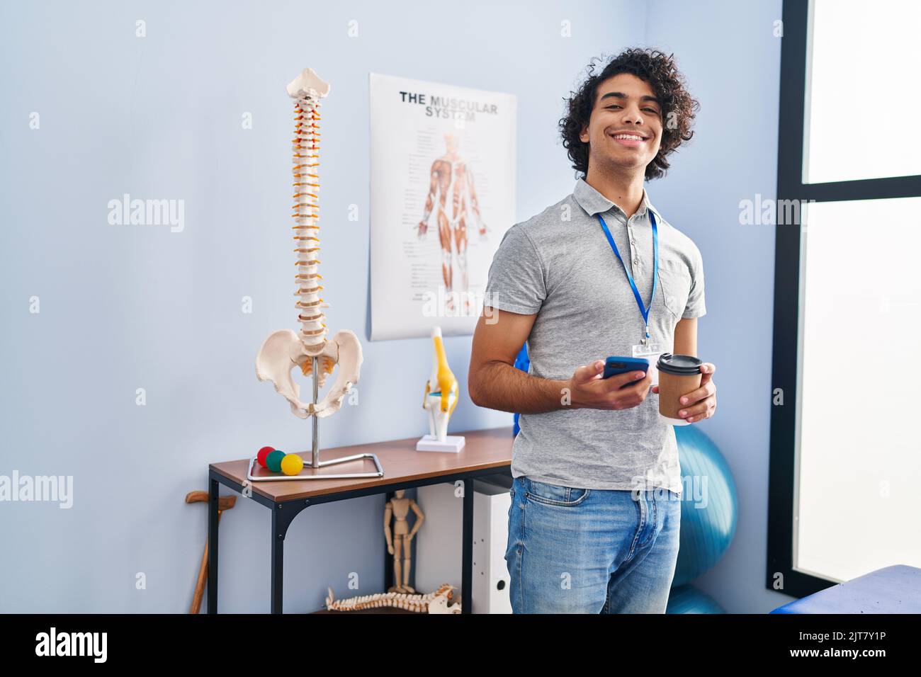 Young hispanic man physiotherapist using smartphone and drinking coffee ...