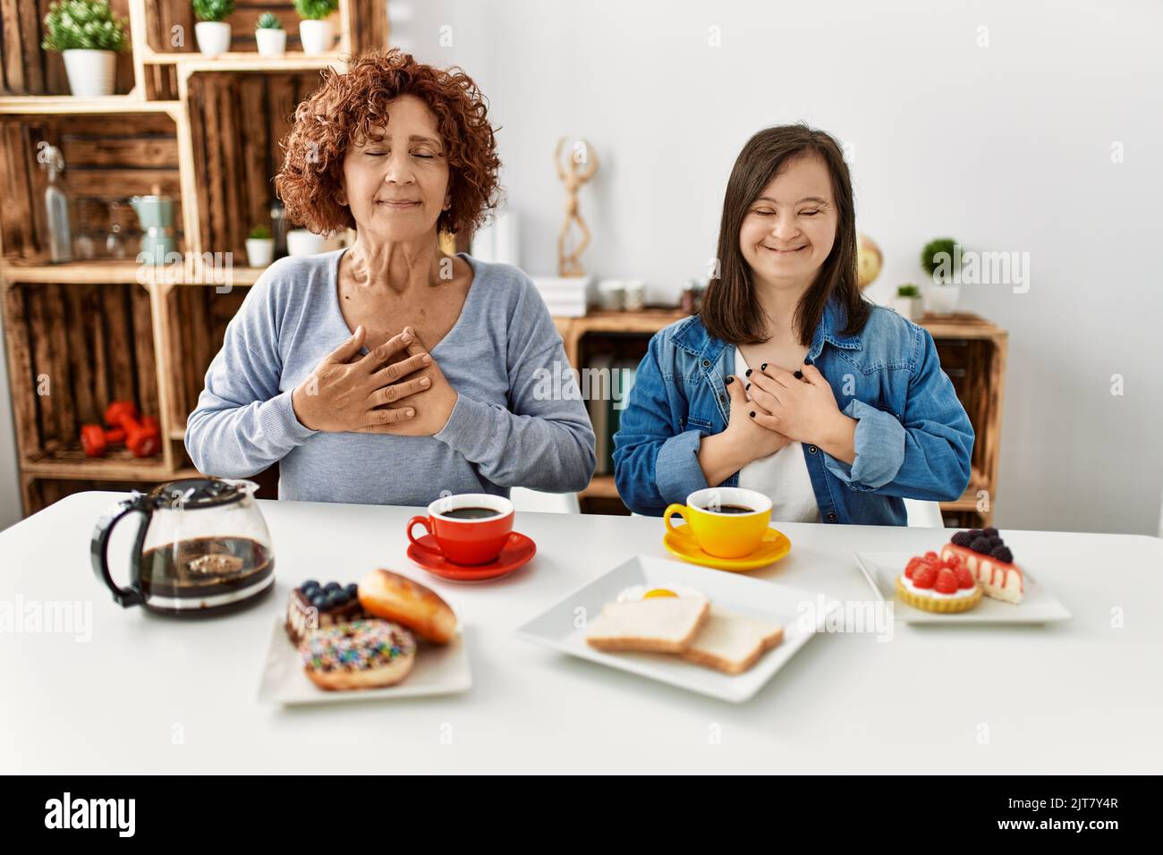 Family of mother and down syndrome daughter sitting at home eating ...