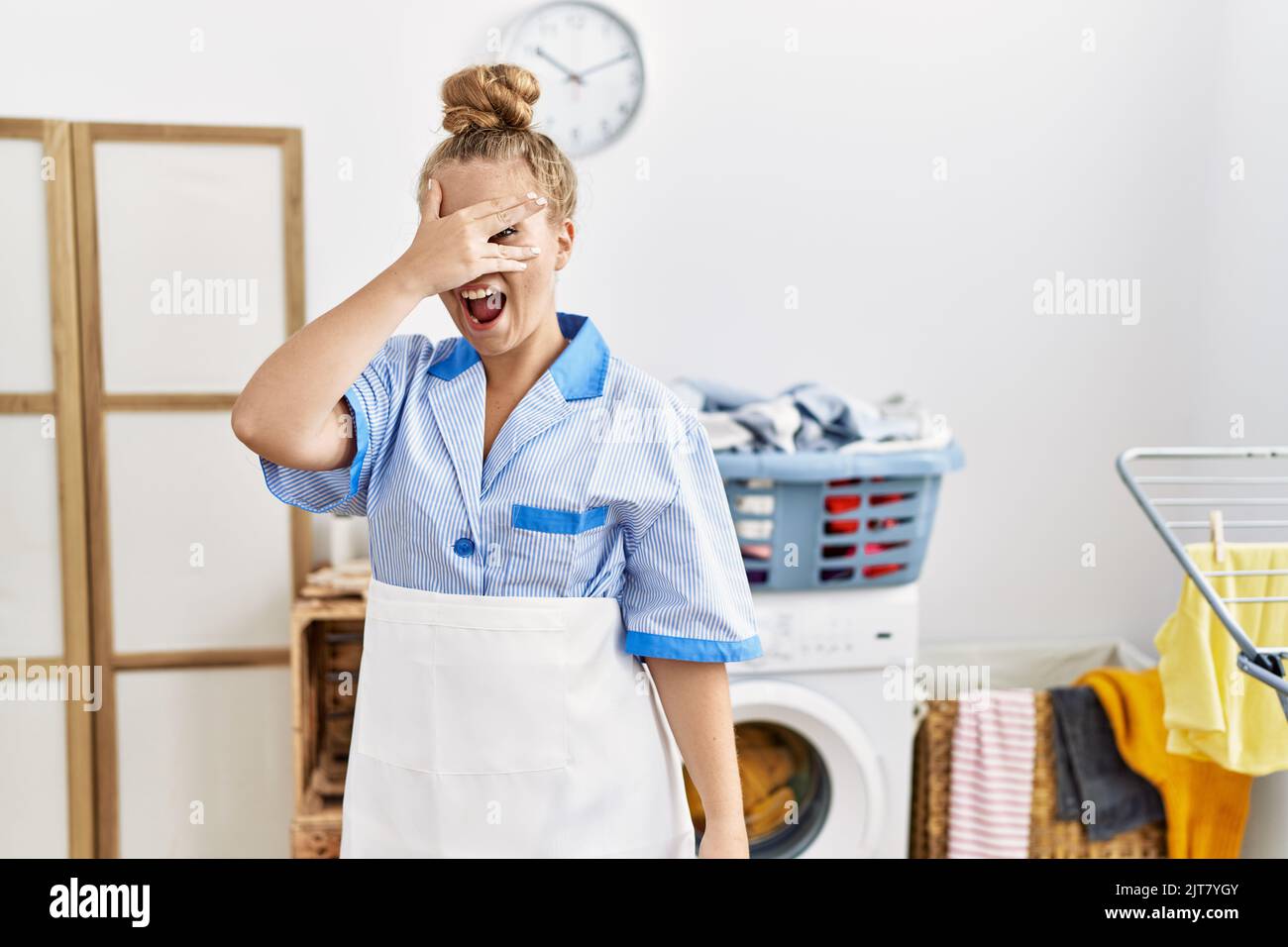 Young caucasian woman wearing cleaner uniform at the laundry room ...