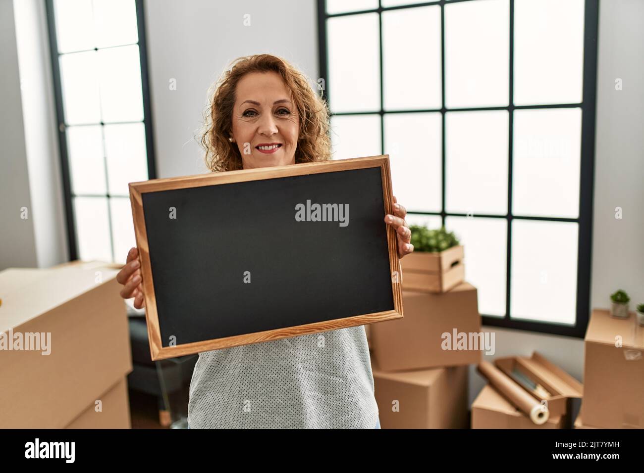 Middle age caucasian woman smiling happy holding empty blackboard at ...