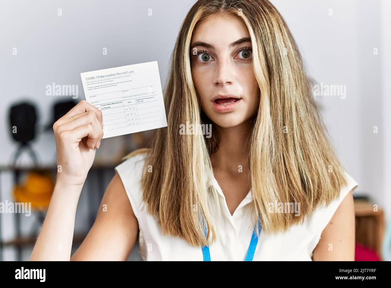 Young blonde woman holding covid record card scared and amazed with ...