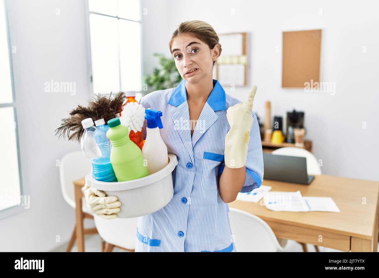 Young blonde woman wearing cleaner uniform holding cleaning products ...