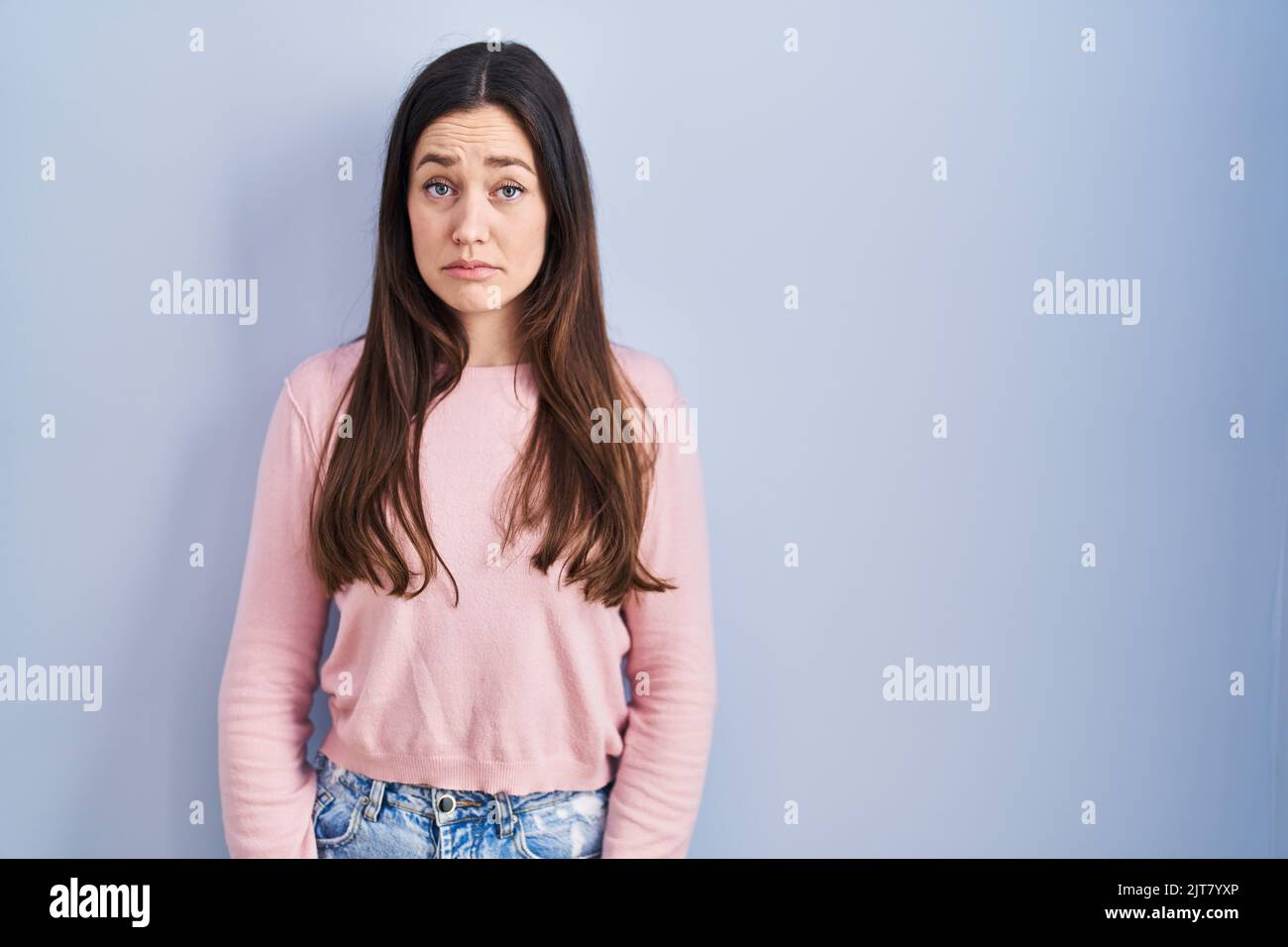 Young brunette woman standing over blue background depressed and worry ...