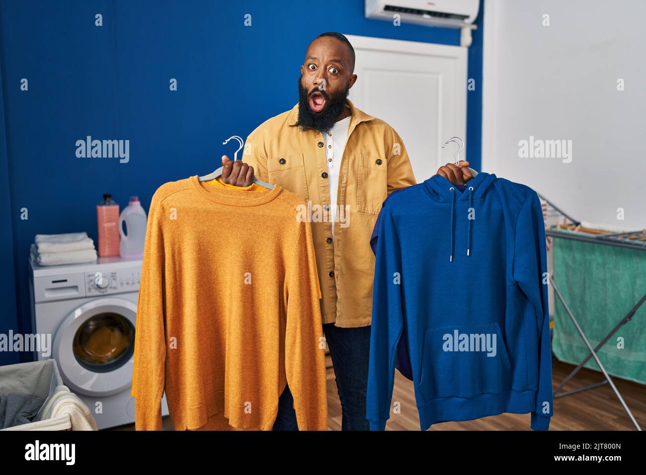 African american man holding clean clothes on hangers at laundry room ...