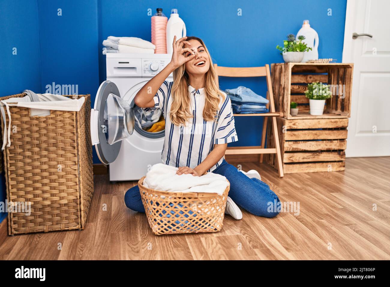 Young blonde woman doing laundry at home smiling happy doing ok sign ...