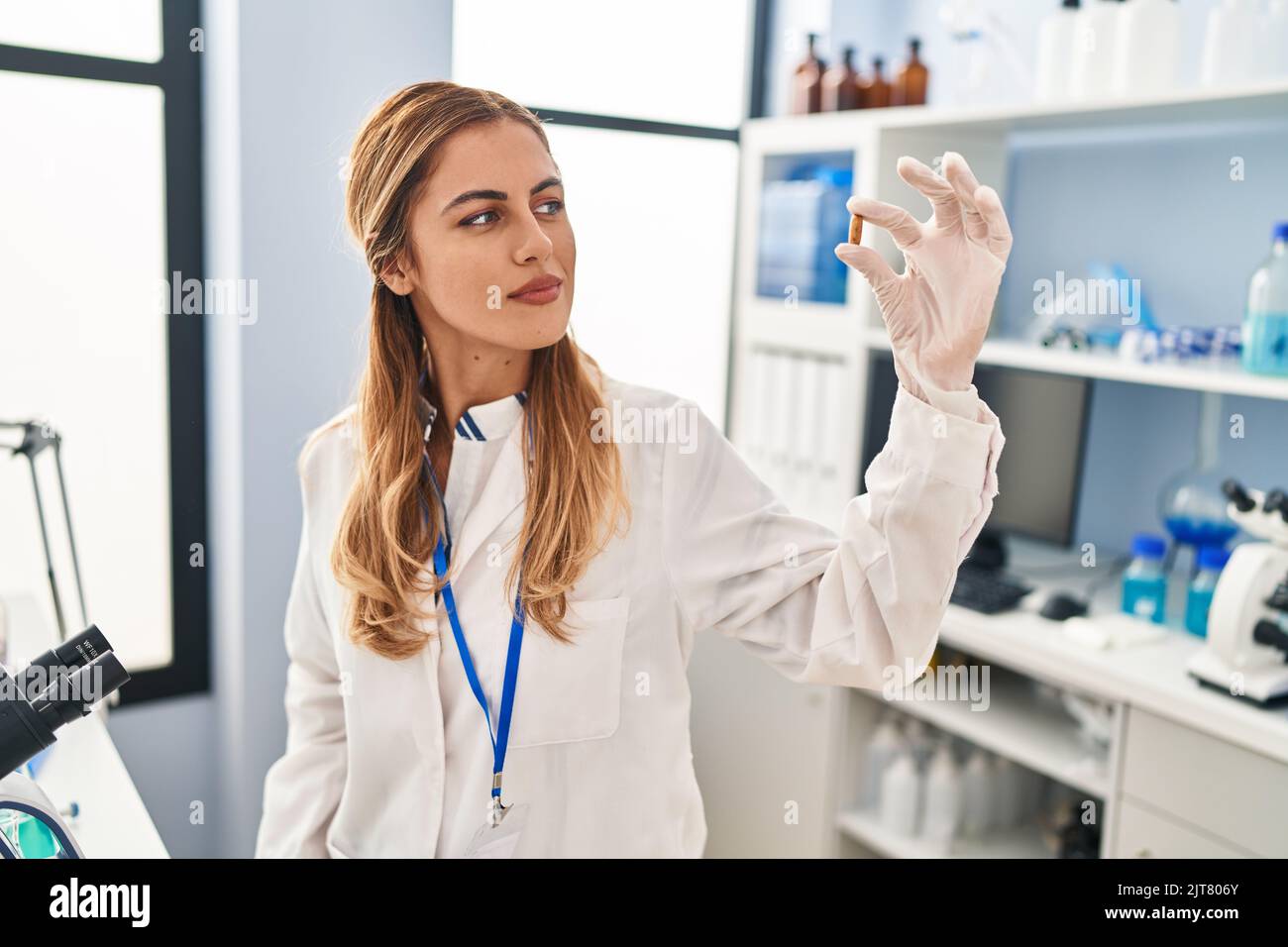 Young blonde woman wearing scientist uniform holding pill at laboratory ...