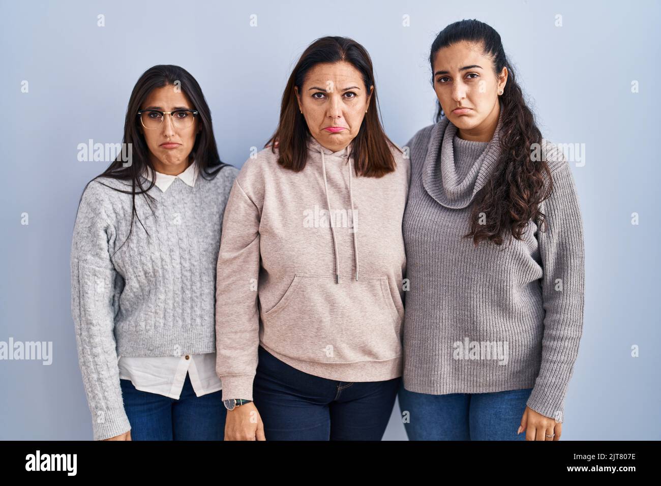 Mother and two daughters standing over blue background depressed and ...