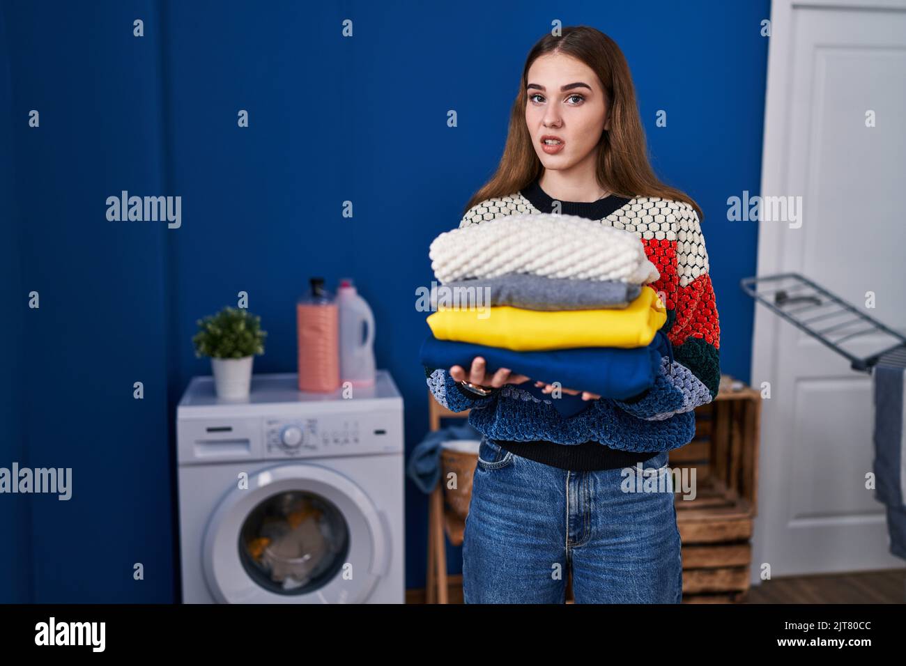 Young hispanic girl holding clean laundry in shock face, looking ...