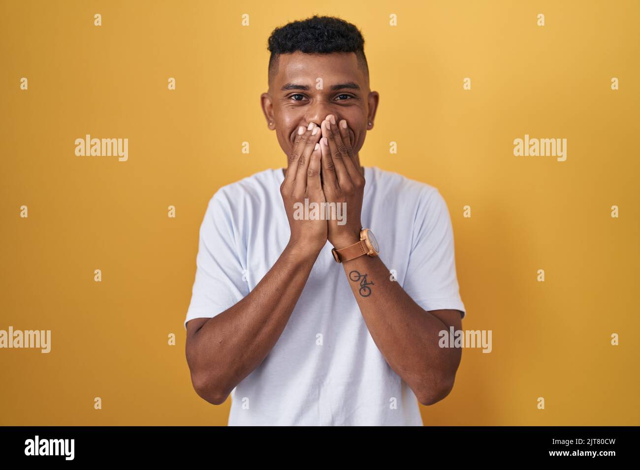 Young hispanic man standing over yellow background laughing and ...
