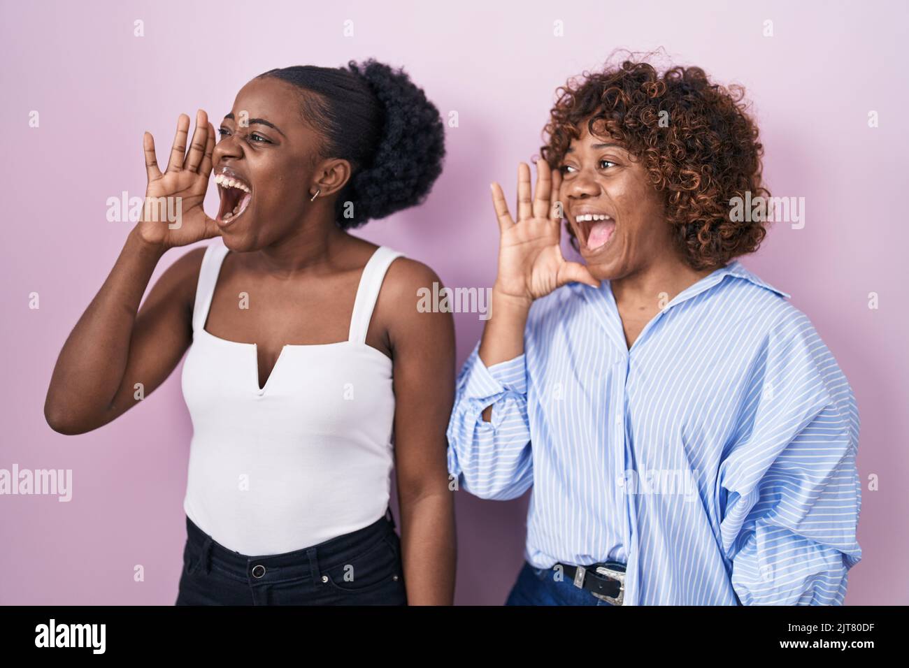 Two african women standing over pink background shouting and screaming ...