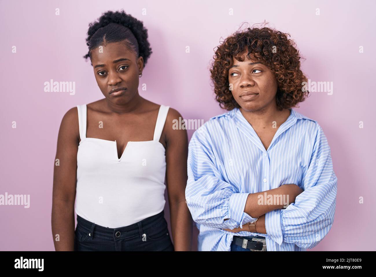 Two african women standing over pink background looking sleepy and ...
