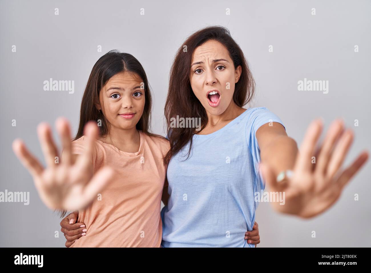 Young mother and daughter standing over white background doing stop ...