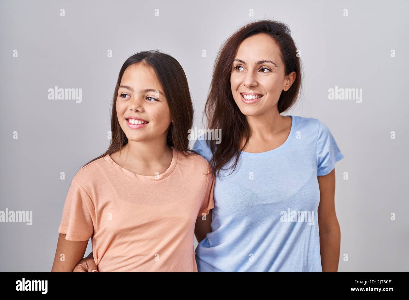 Young mother and daughter standing over white background looking away ...