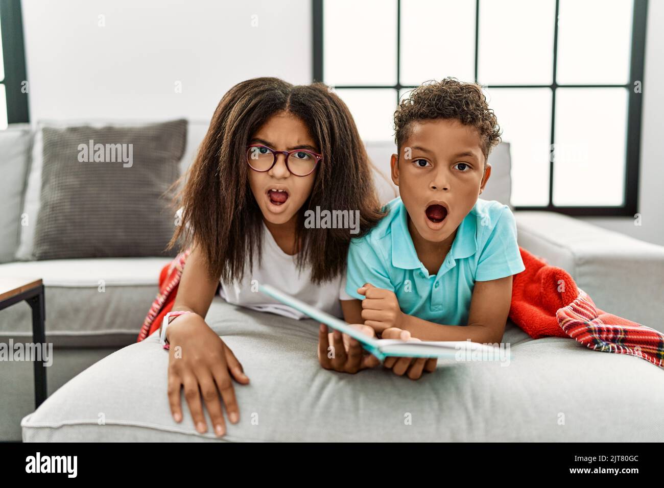 Two siblings lying on the sofa reading a book in shock face, looking ...