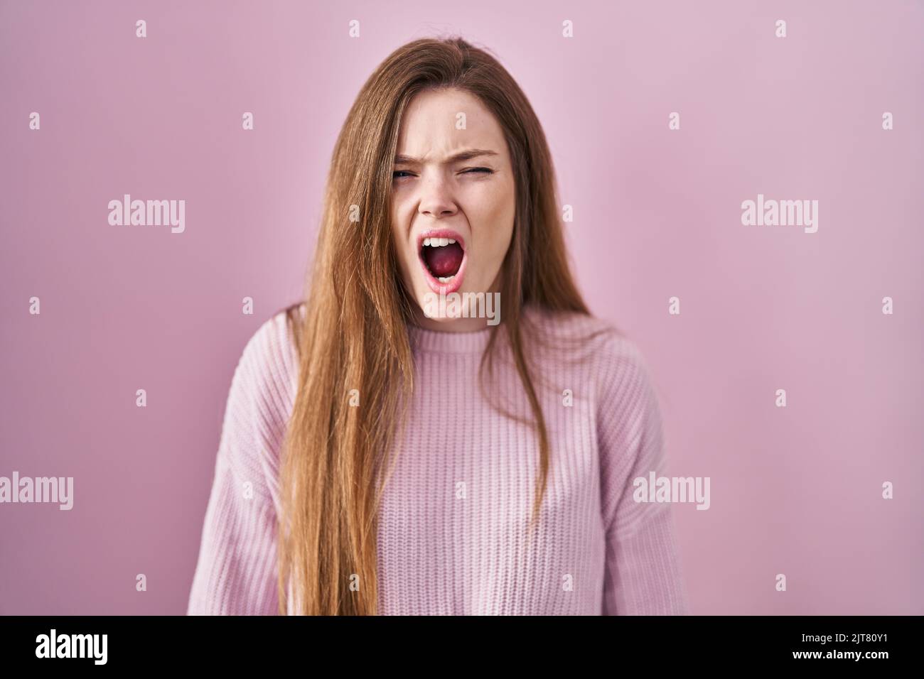 Young caucasian woman standing over pink background angry and mad ...