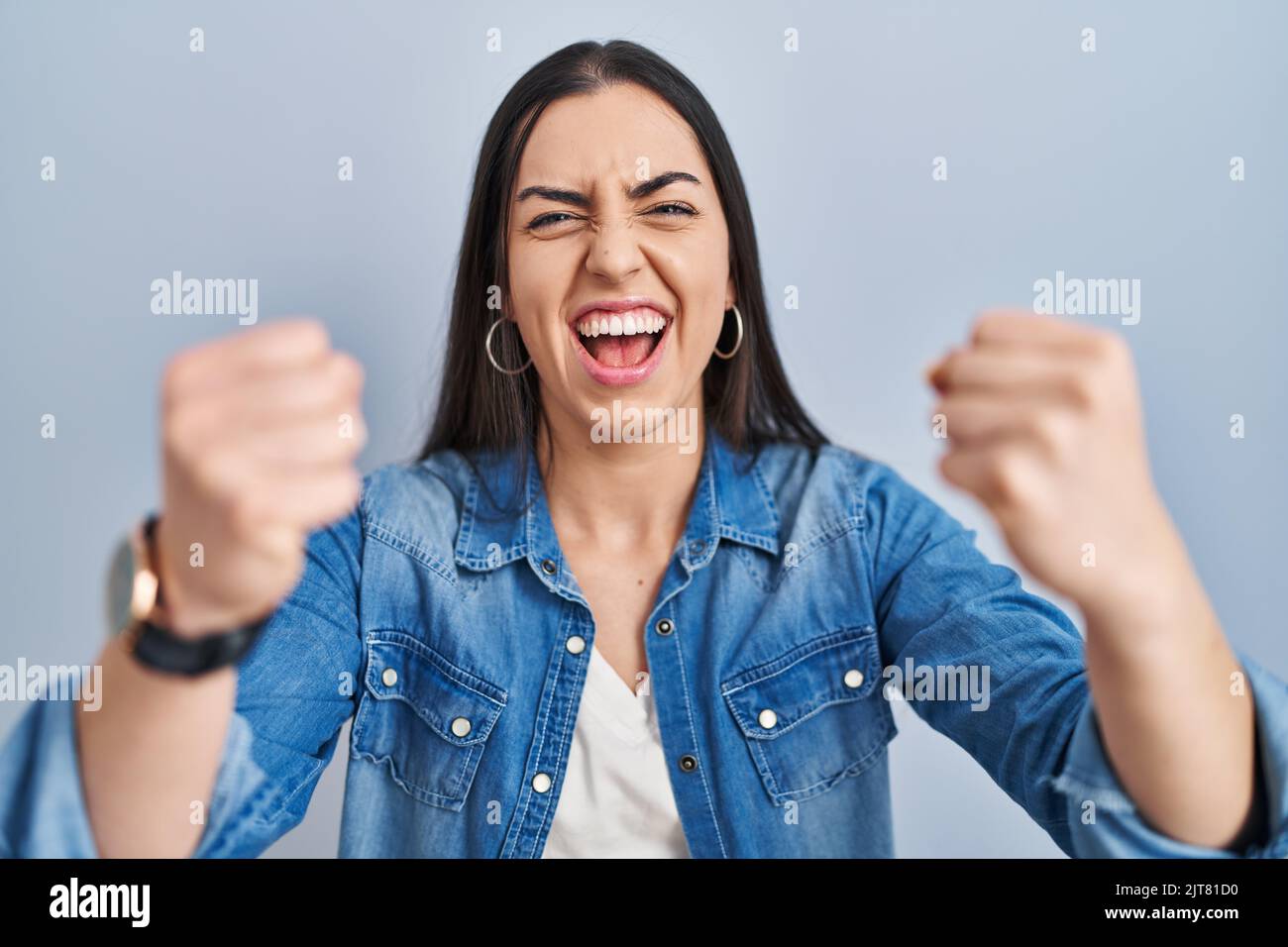 Hispanic woman standing over blue background angry and mad raising ...