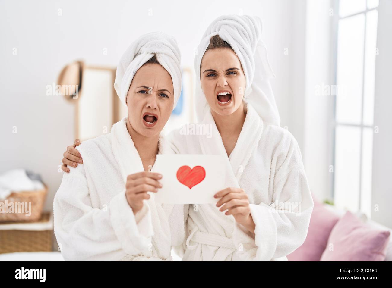 Middle age woman and daughter wearing bath robe holding heart card ...