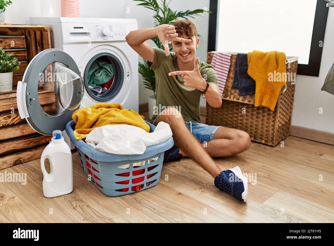 Young caucasian man putting dirty laundry into washing machine smiling ...