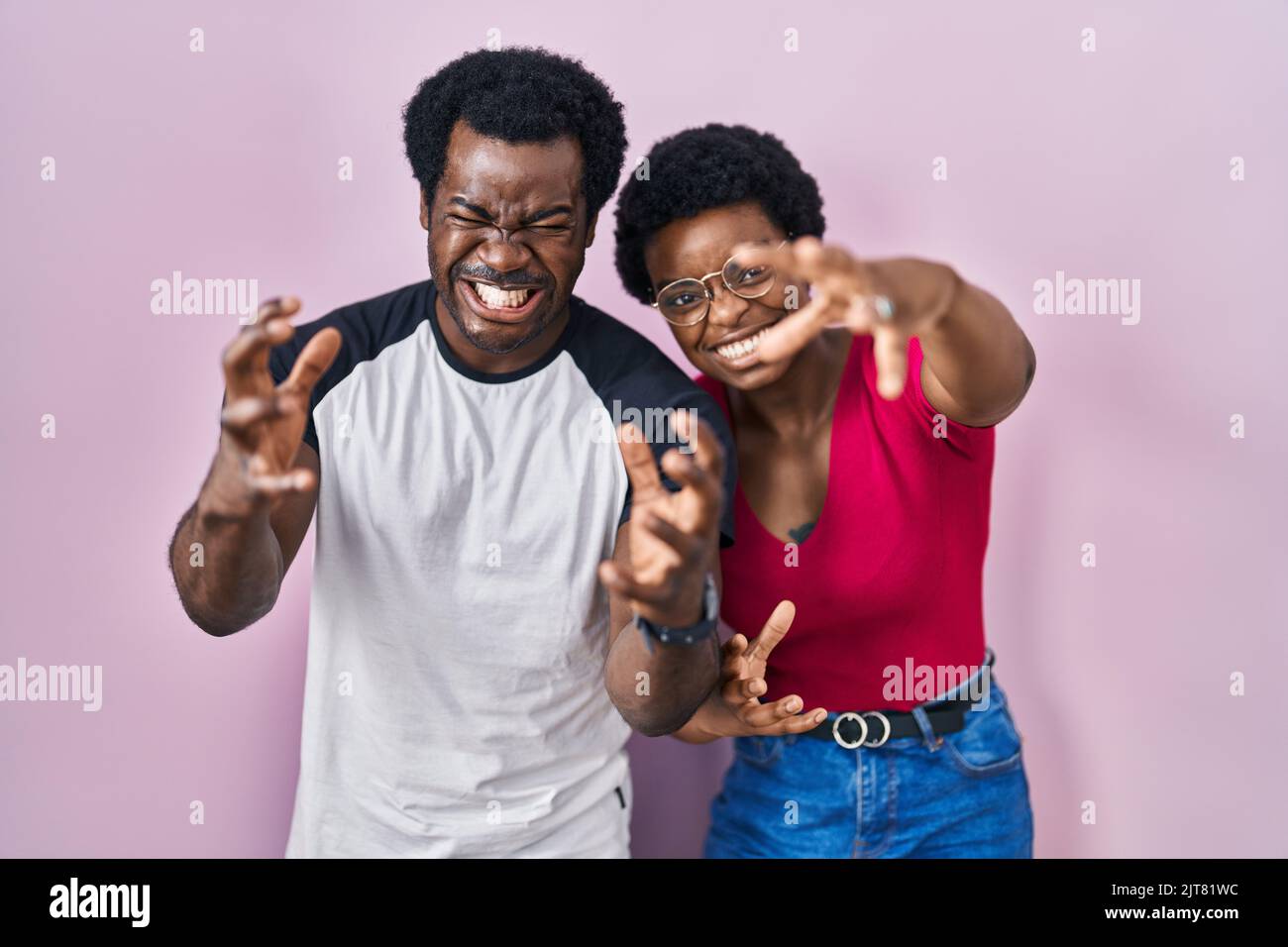 Young african american couple standing over pink background shouting ...