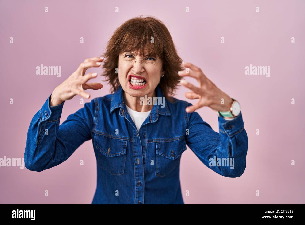 Middle age woman standing over pink background shouting frustrated with ...