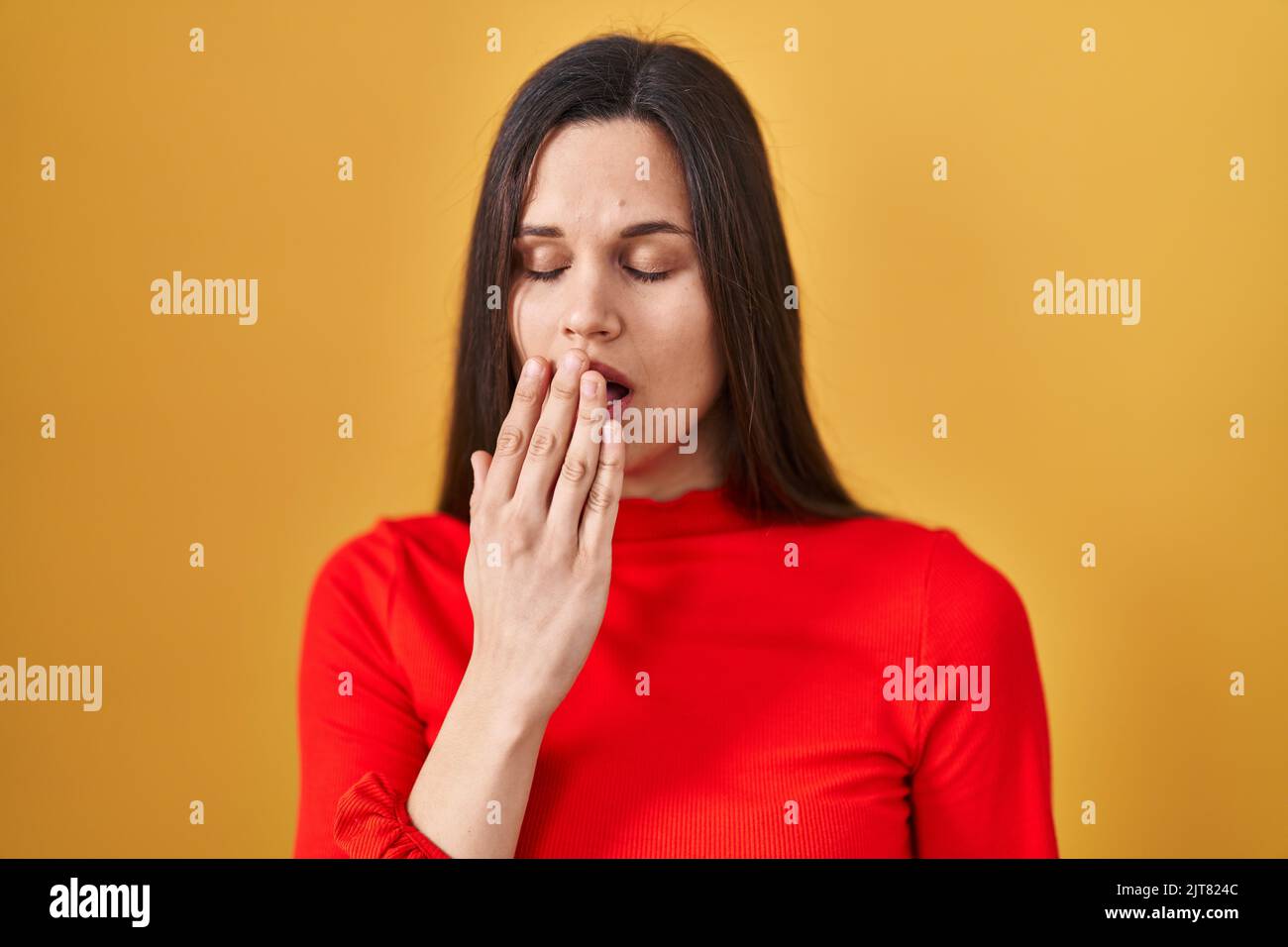 Young hispanic woman standing over yellow background bored yawning ...