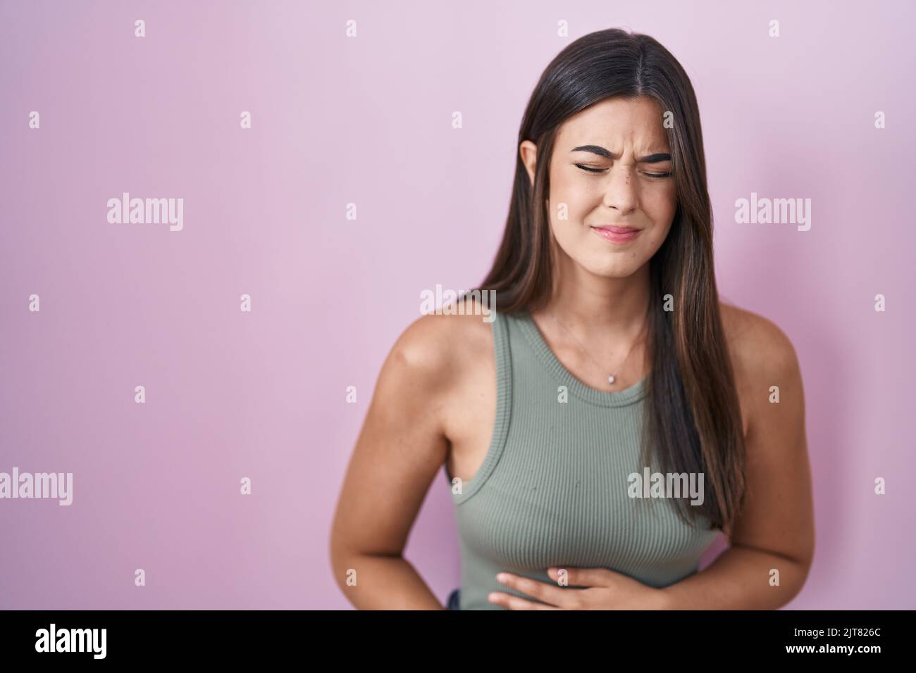 Hispanic woman standing over pink background with hand on stomach ...
