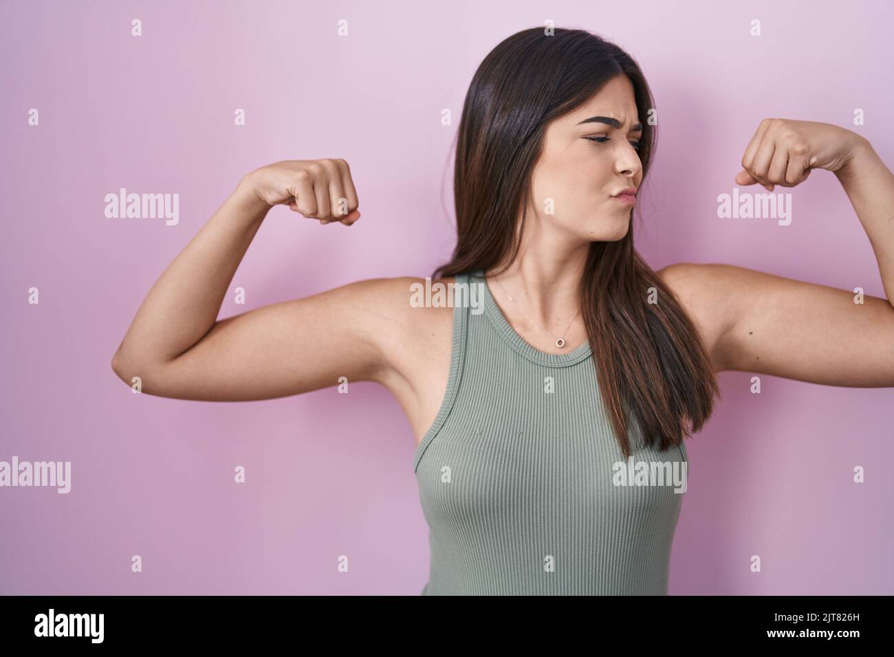 Hispanic woman standing over pink background showing arms muscles ...