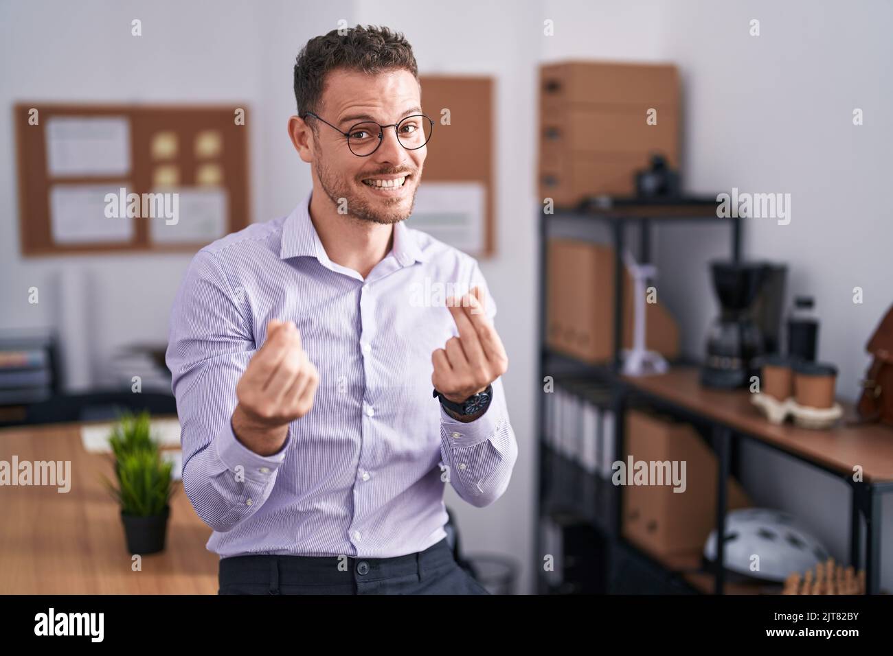 Young hispanic man at the office doing money gesture with hands, asking ...
