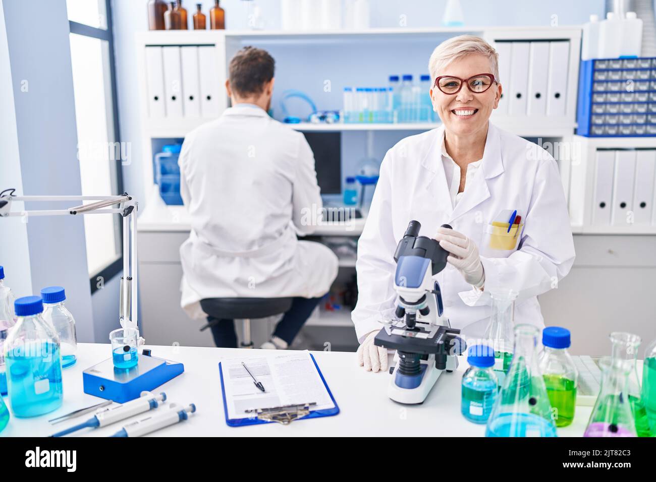 Middle age woman working at scientist laboratory looking positive and ...