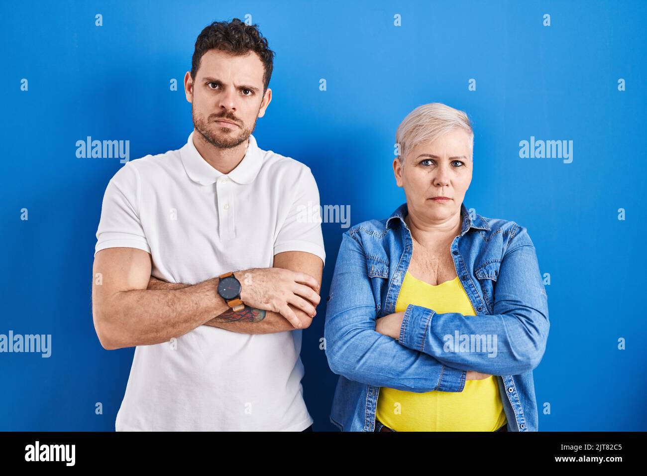Young brazilian mother and son standing over blue background skeptic ...