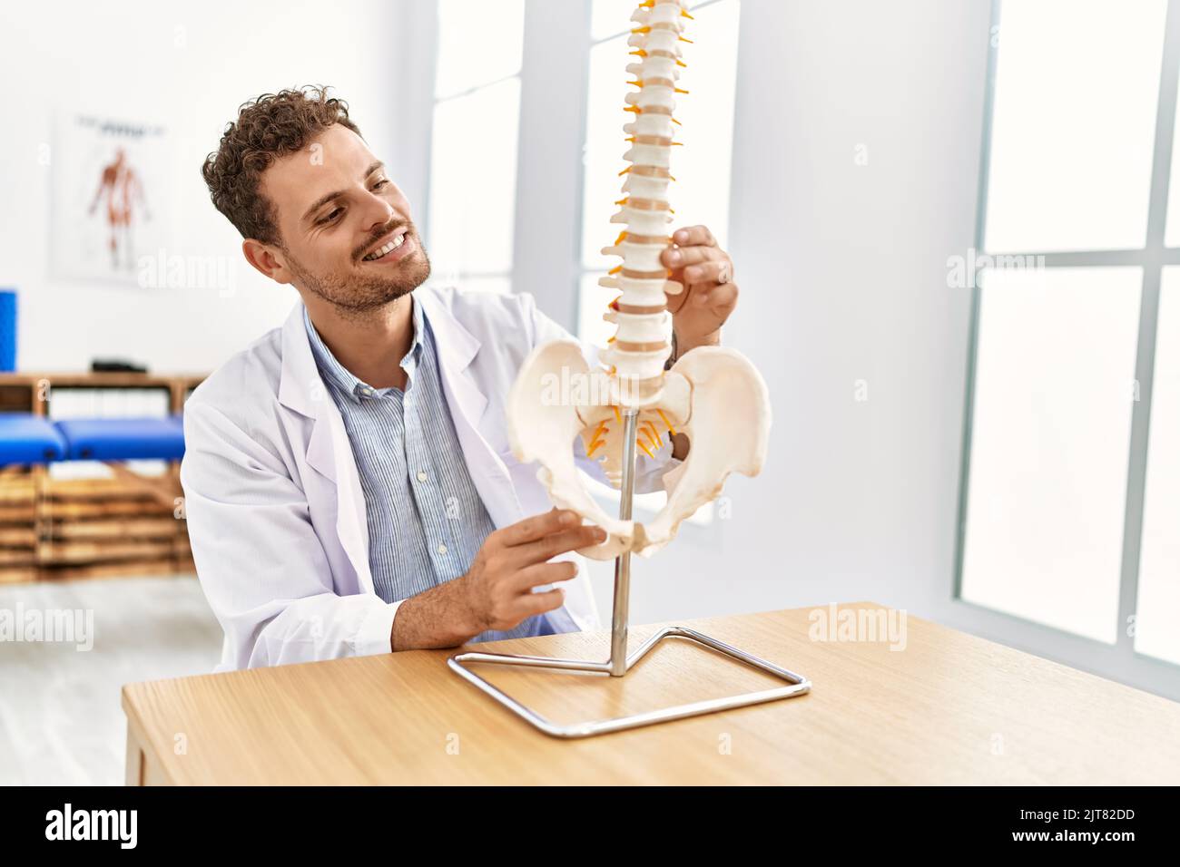 Young hispanic man wearing physiotherapist uniform touching anatomical ...