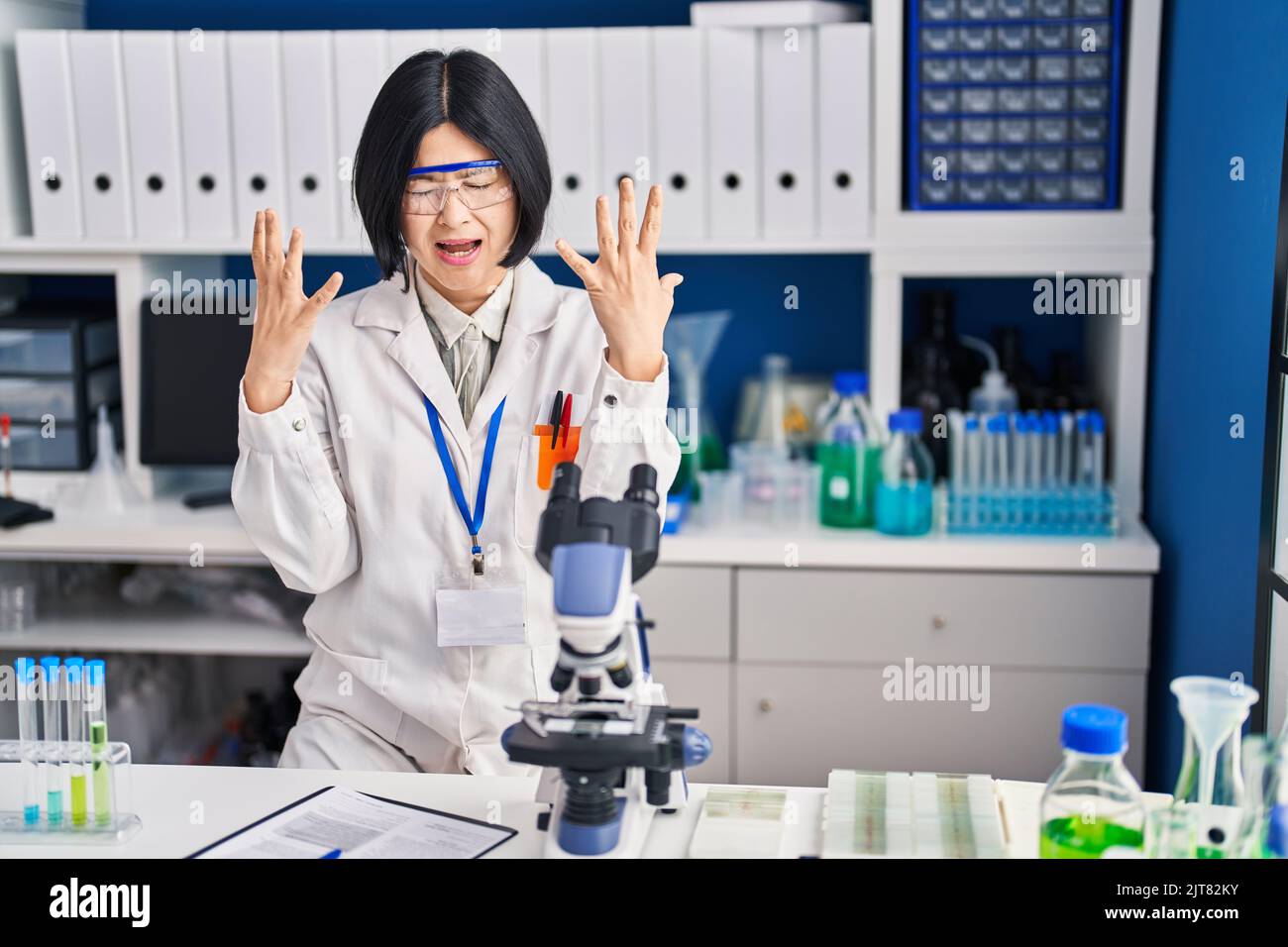 Young asian woman working at scientist laboratory celebrating mad and ...
