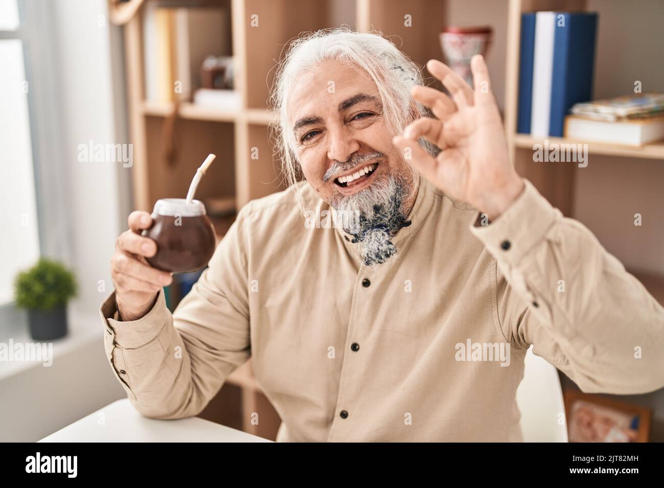 Middle age man with grey hair drinking mate infusion doing ok sign with ...