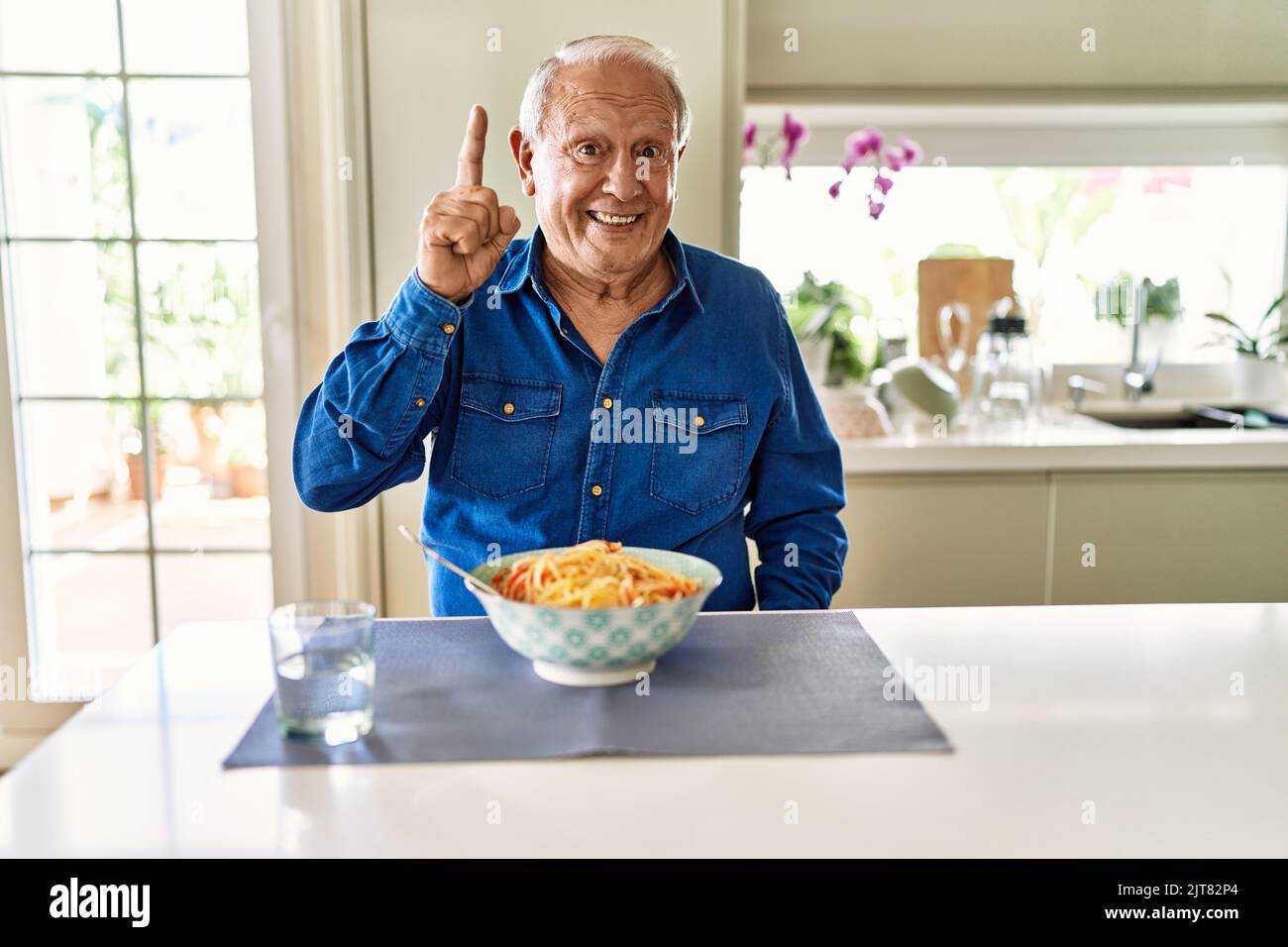 Senior man with grey hair eating pasta spaghetti at home pointing ...