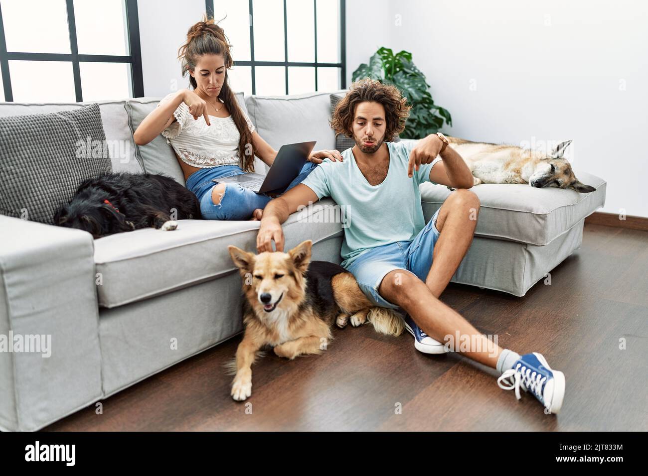 Young hispanic couple with dogs relaxing at home pointing down looking ...